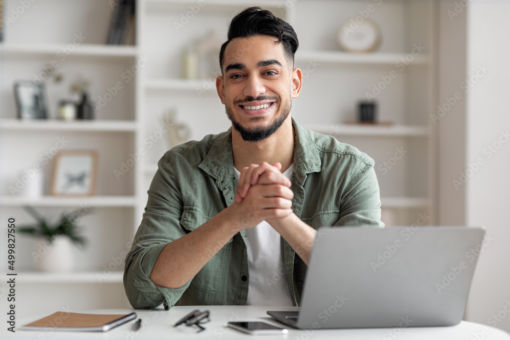 Glad handsome young islamic man with beard at workplace with laptop in ...