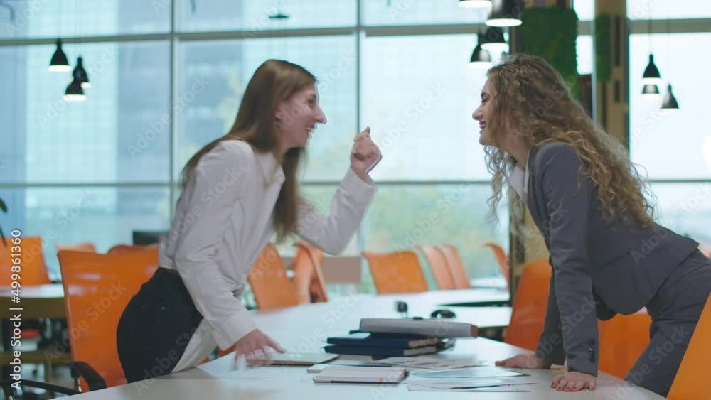 Young women whispering on ear gossiping in office indoors laughing ...