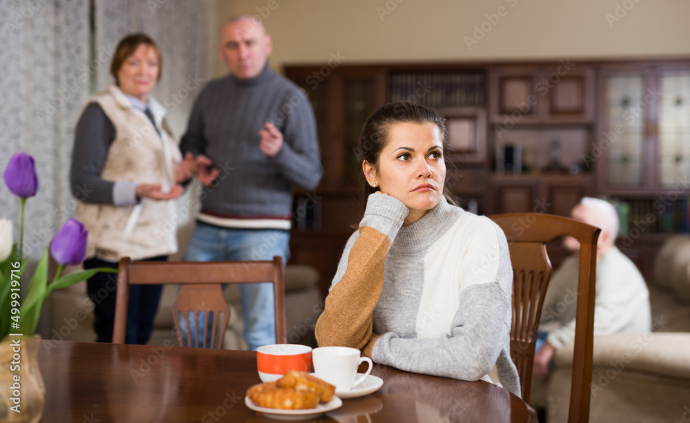 Offended woman sitting by table while her husband and senior parents ...