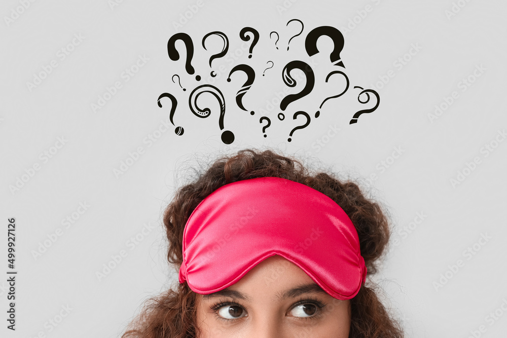 Young African-American woman with sleep mask and question marks on grey ...