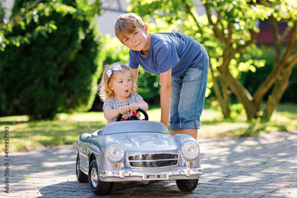 Two happy children playing with big old toy car in summer garden ...