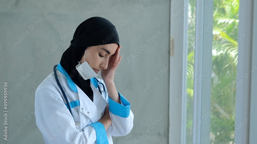 A Muslim woman doctor stands by a window in the office. Removes the ...