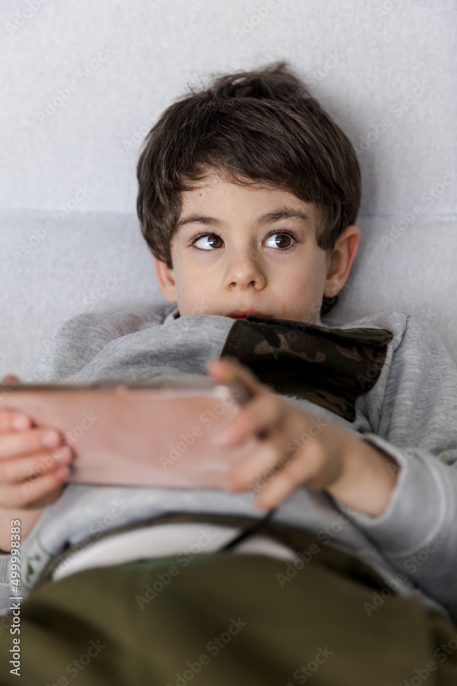Autistic boy with a lost look sitting on the sofa at home while holding ...