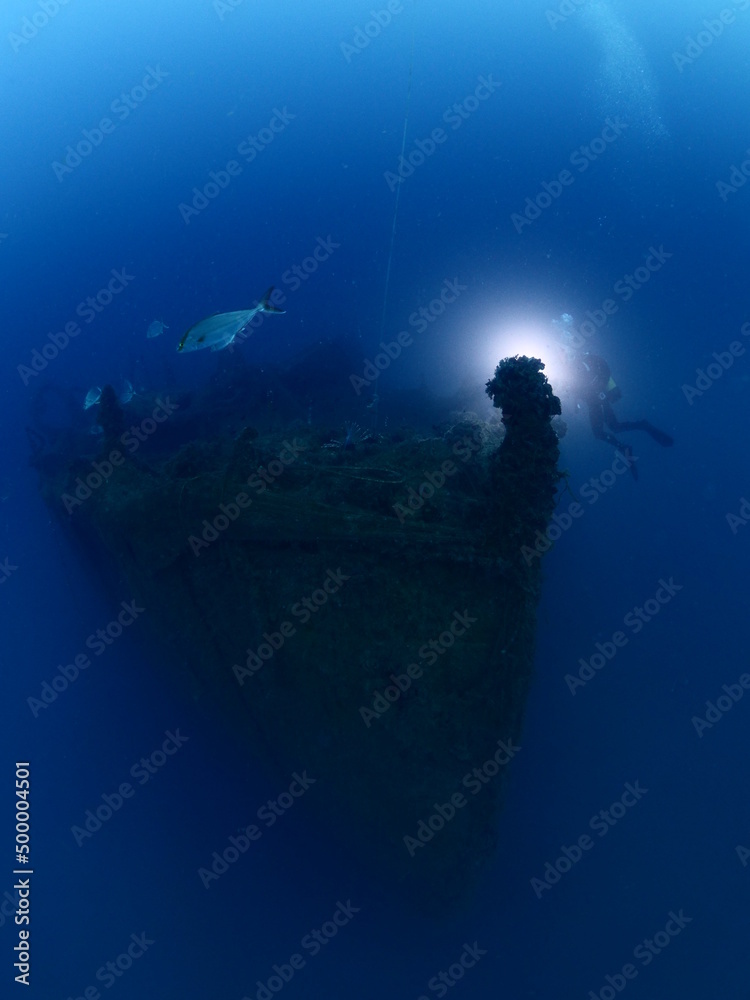 scuba divers exploring old ship wreck with torch light underwater from ...