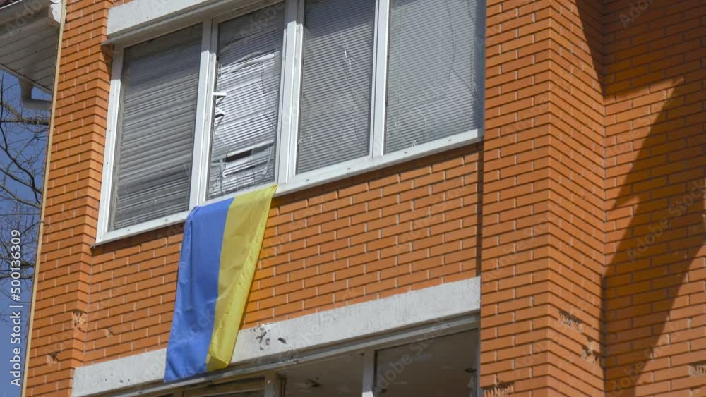 Ukrainian flag hangs on balcony of a shelled house in Ukraine. Shelling ...