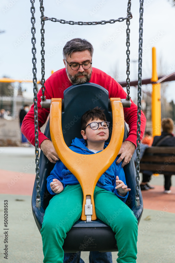 A relaxed child with a disability playing on adapted swing with his dad ...