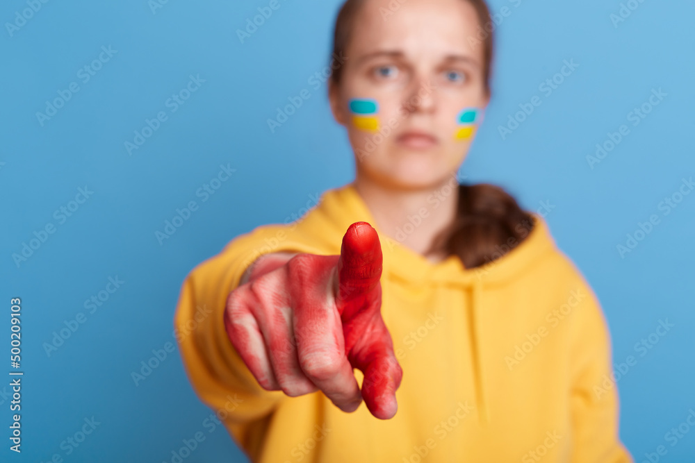 Sad woman in yellow hoodie with Ukrainian flag on cheeks, posing ...