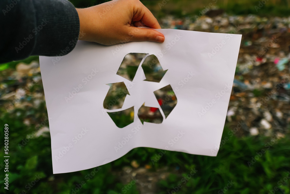 Defocus hand holding cut paper with the logo of recycling on dump ...