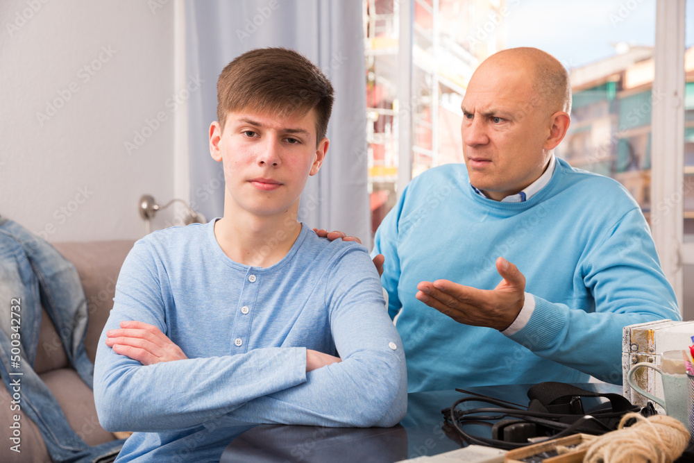 Angry father scolding his turned away son teenager at home Stock Photo ...