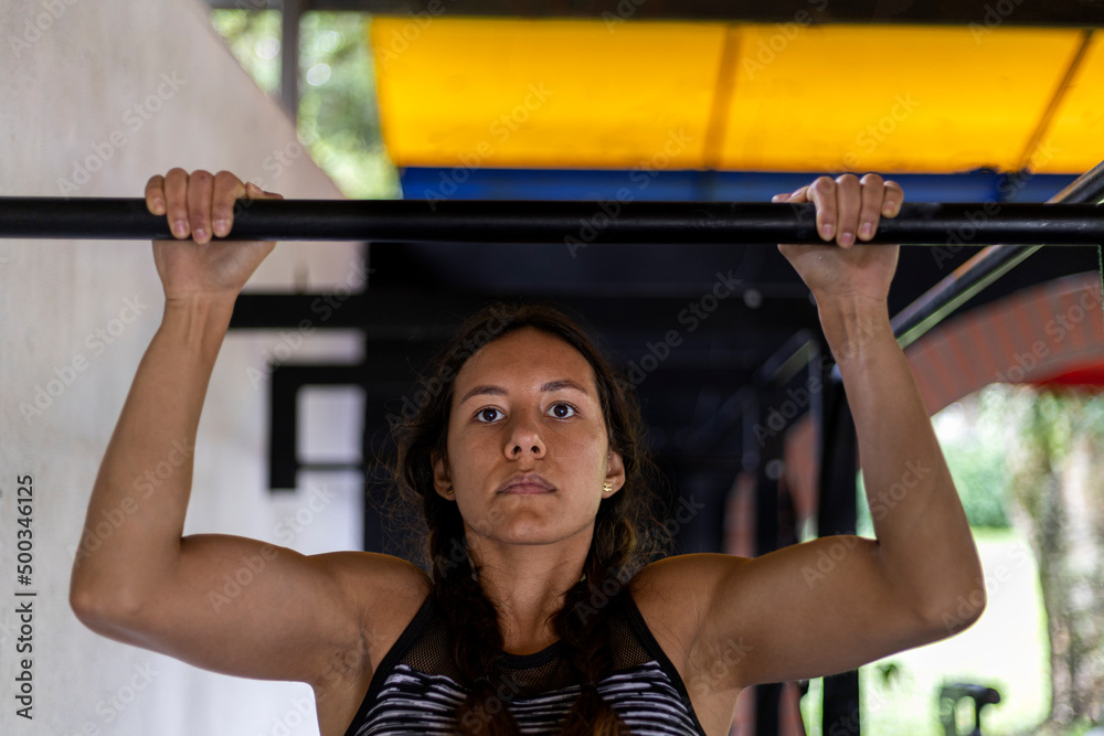 Young Latin American woman tests her arm strength on the calisthenics ...
