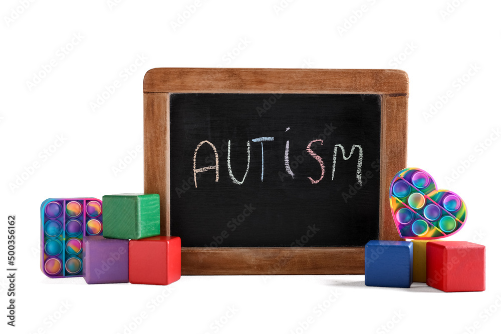 Chalkboard with word AUTISM, cubes and pop it fidget toys on white ...