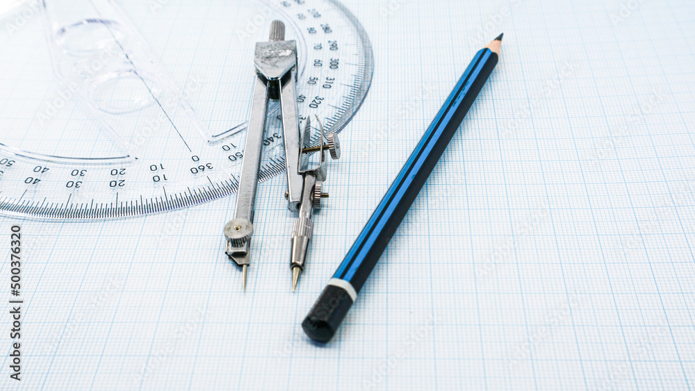 On blue graph paper are compasses, protractor, ruler, and a pencil ...