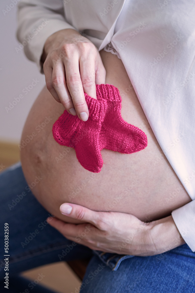 A pregnant woman holds pink handmade socks knitted from threads in her ...