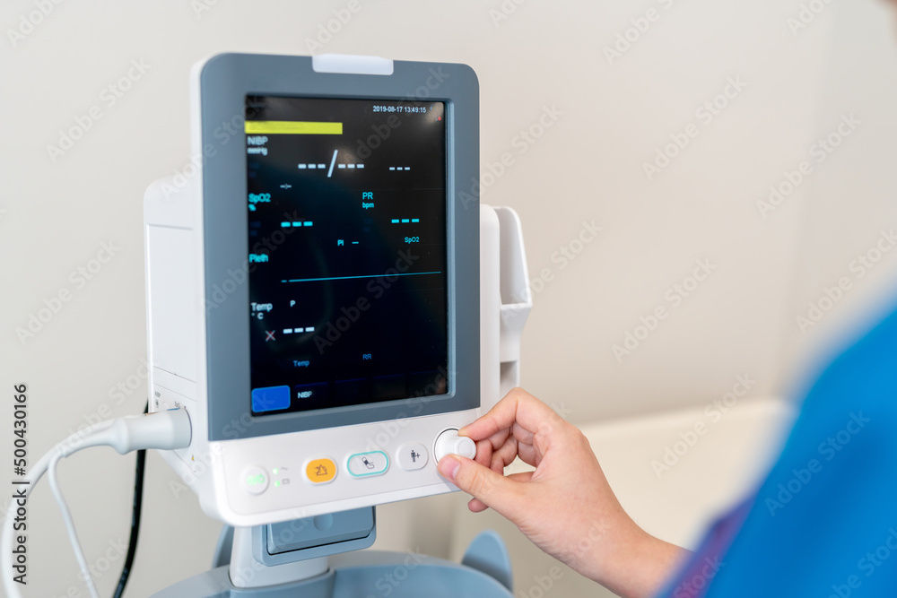 Doctor operating vital sign monitor in patient room of modern hospital ...