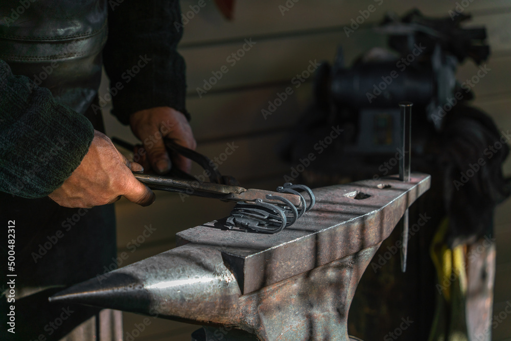 Selective focus closeup of a blacksmith's hand with a tool and a metal ...