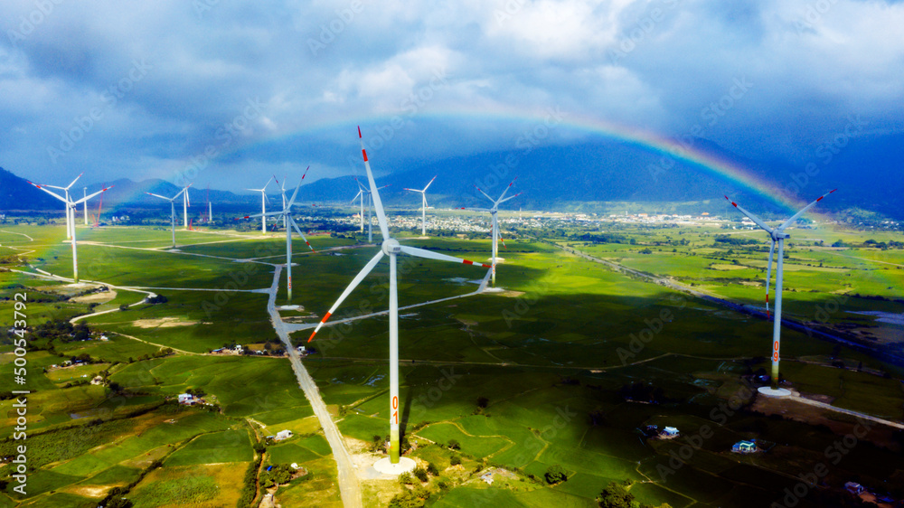 Wind turbine towers in a green field under the blue sky with rainbow ...
