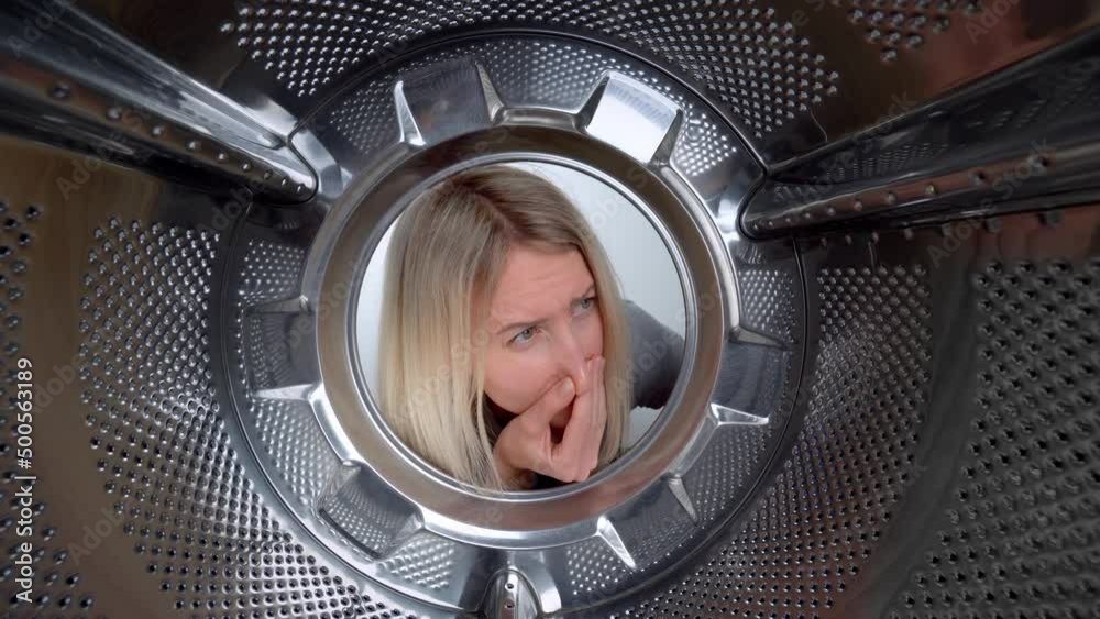 Smelly washing machine and laundry room. Young blonde woman looks ...