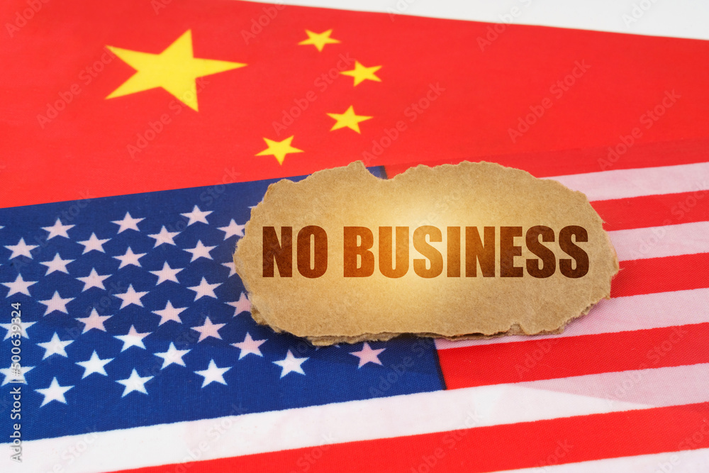 On the flags of the USA and China lies a cardboard sign with the ...