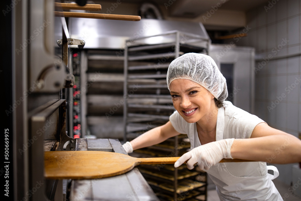 Portrait of smiling female baker in white uniform and hairnet working ...
