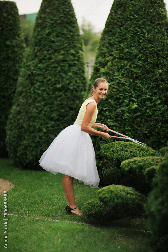 Beautiful woman girl in a dress with garden scissors cuts juniper ...