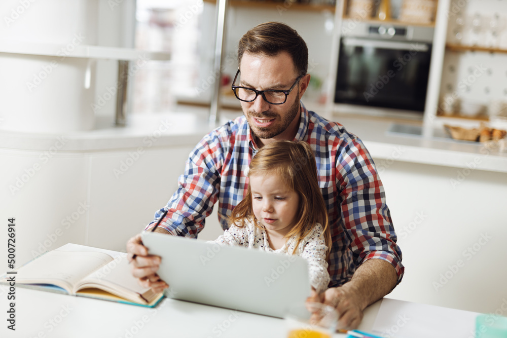 Young father using computer while his little girl sitting on his lap at ...