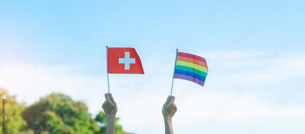 hands showing LGBTQ Rainbow and Switzerland flag on nature background ...