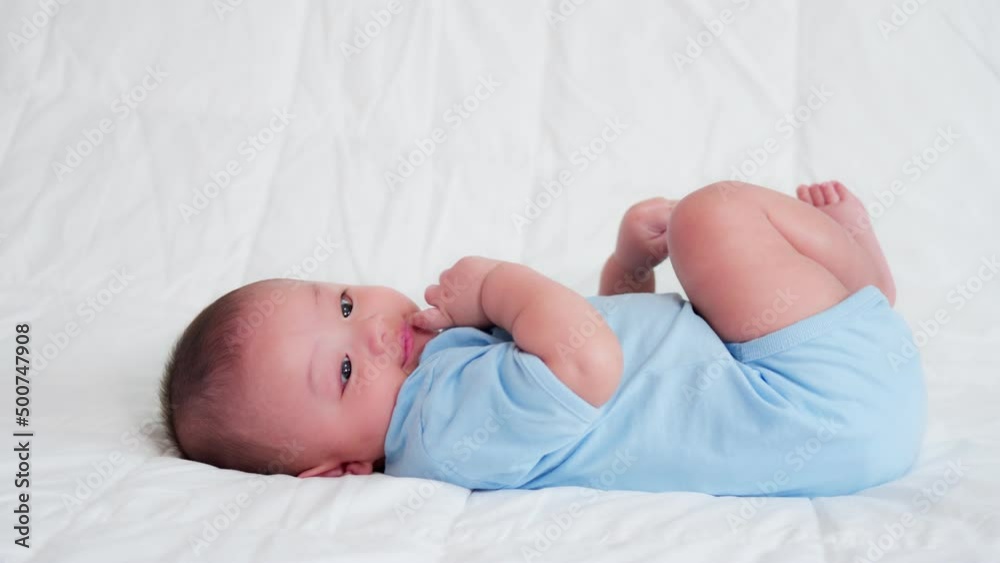 Happy family, Cute Asian newborn baby wear blue shirt lying play on white bed looking at camera ...