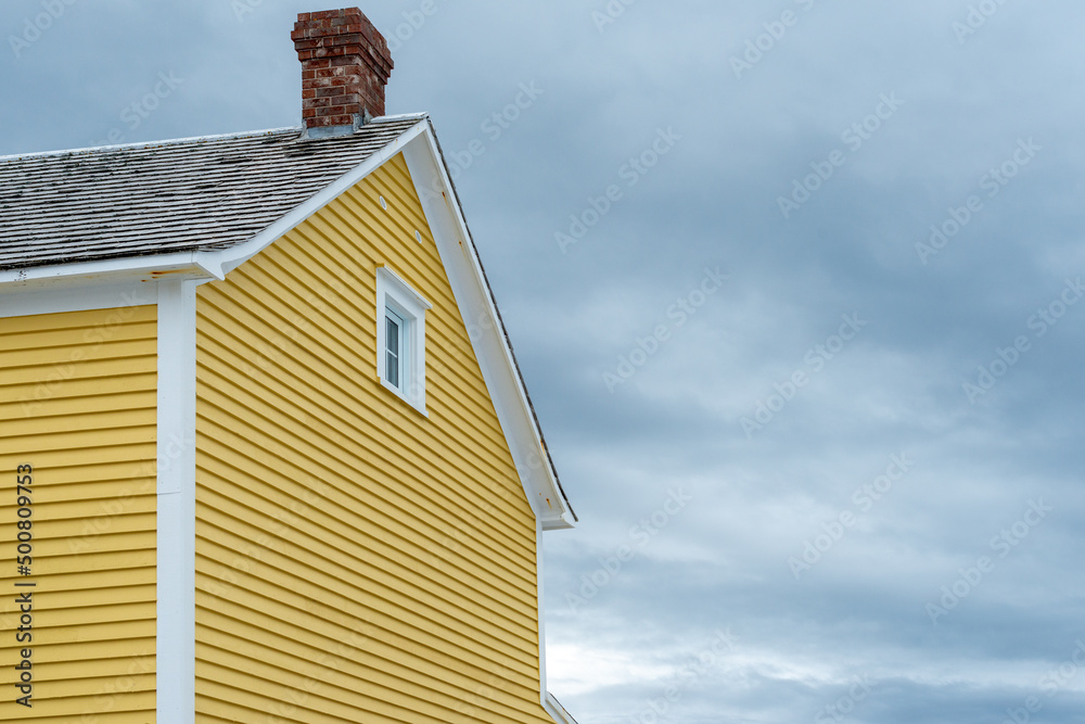 A tall yellow wooden building with white trim, a small glass window ...