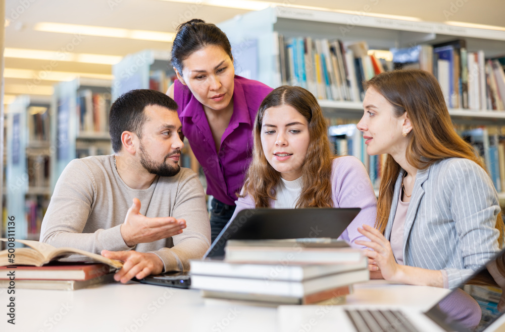 Cheerful young adult university students studying in library using ...