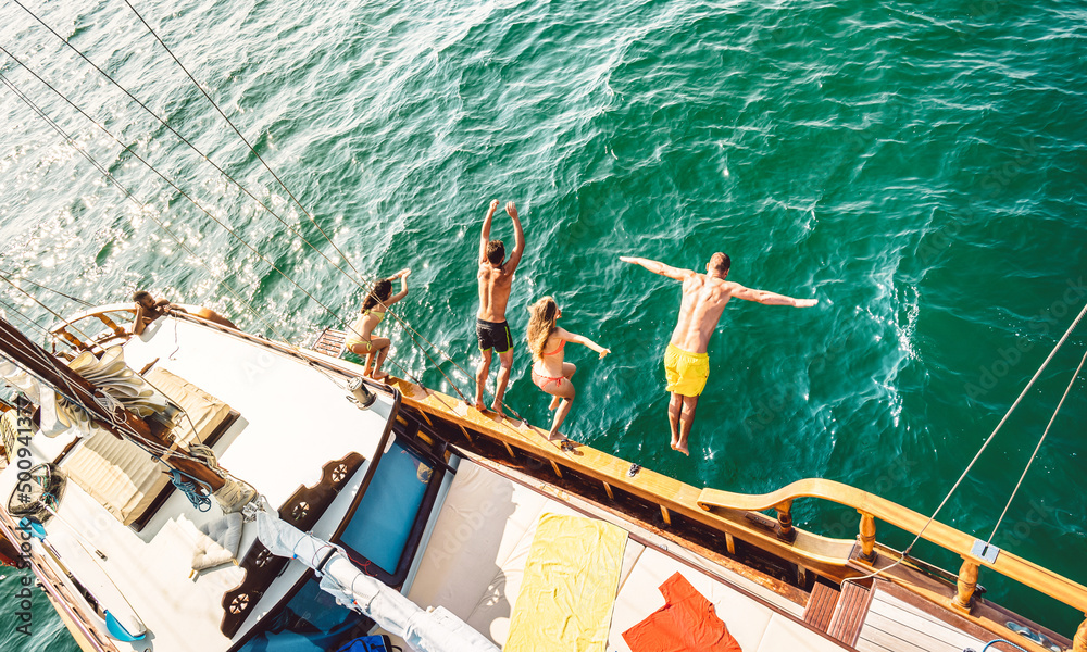Top view of trendy adventurous friends jumping from sailboat on sea ...
