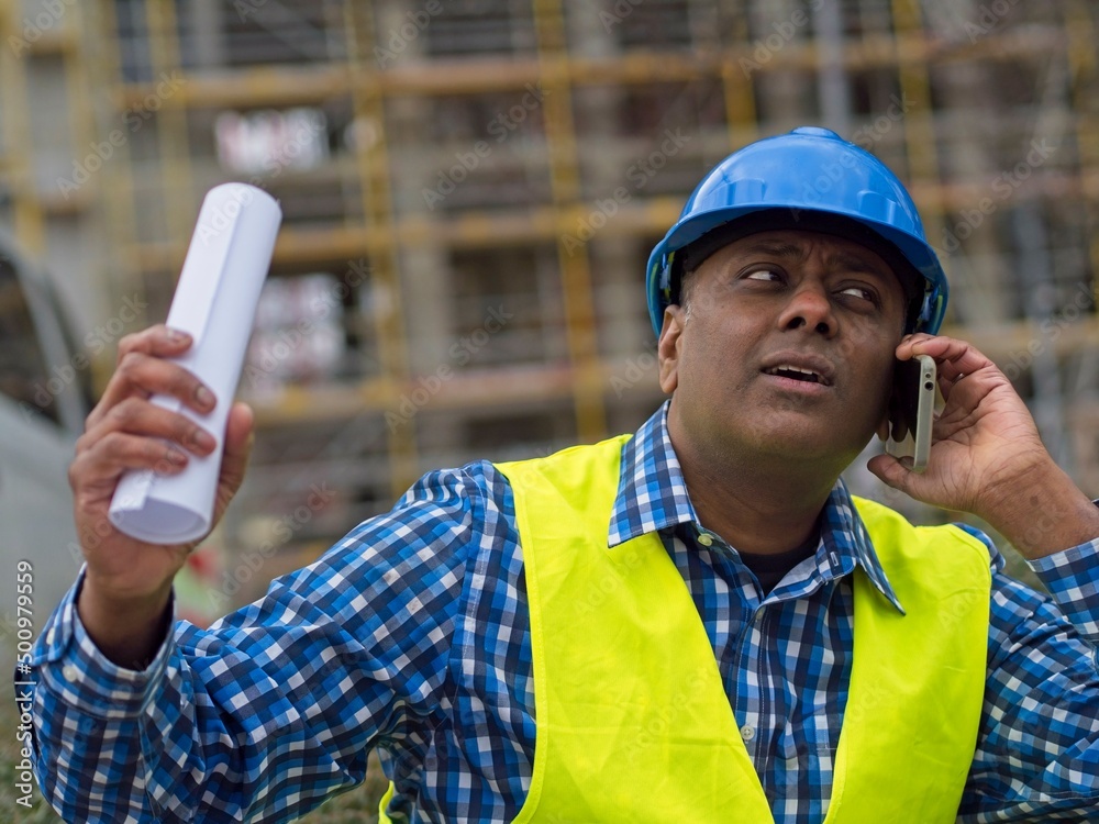 Worried Indian civil engineer with safety jacket and helmet talking on ...