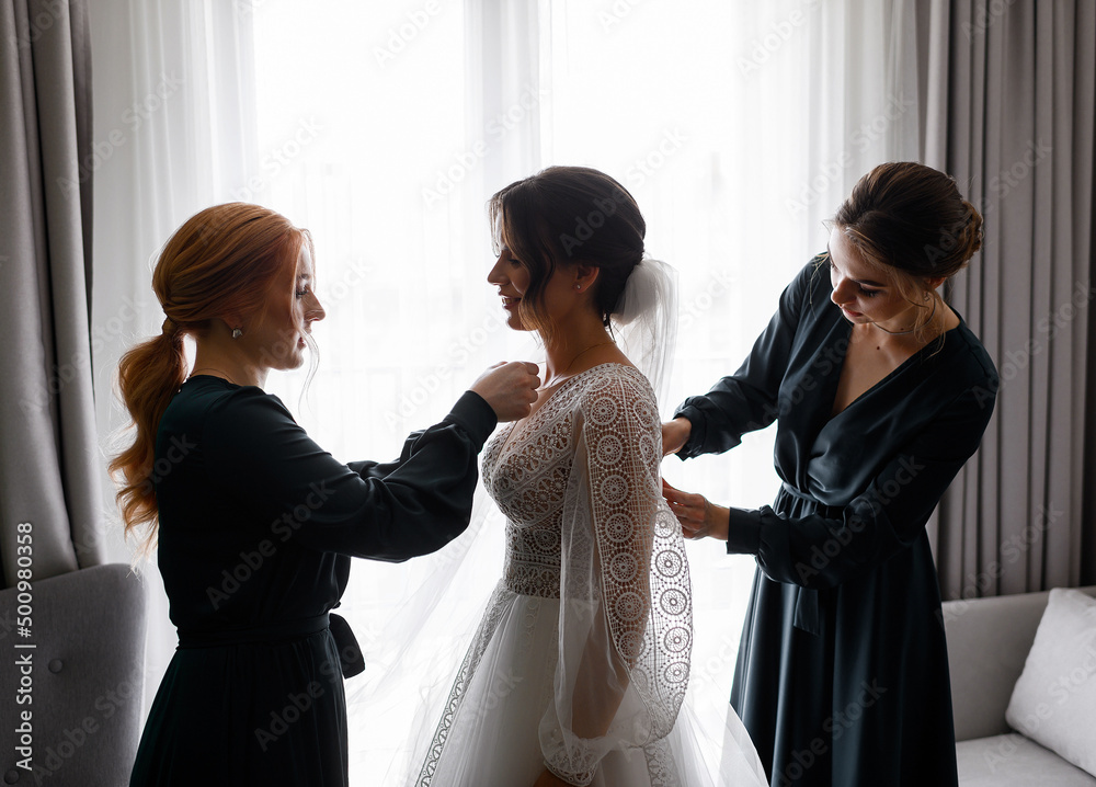 Side view of cheerful and pretty bride, standing near window in room ...