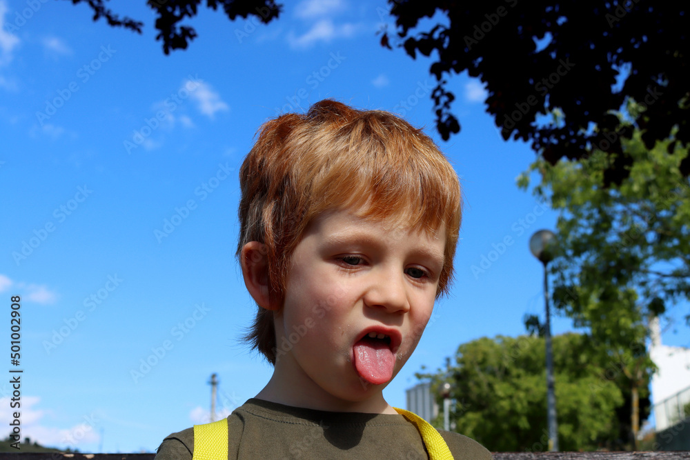 The blond boy sticks out his tongue, looking down. A five-year-old boy ...