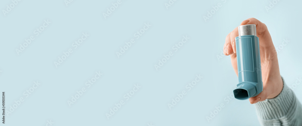 Female hand holding asthma inhaler on light blue background with space ...