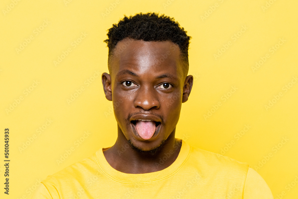 African man sticking his tongue out on yellow color background in light ...