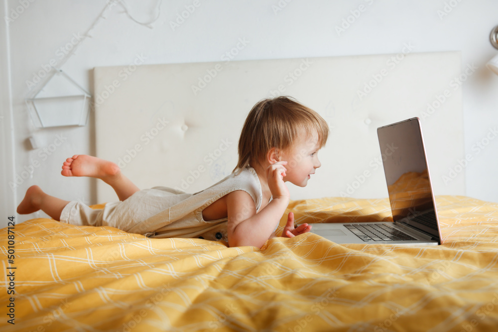 kid with laptop on bed, child presses keys on keyboard, baby toddler ...