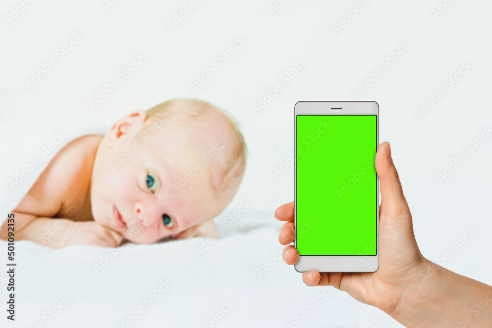 Baby newborn on white bed, woman holding mobile phone with green screen ...