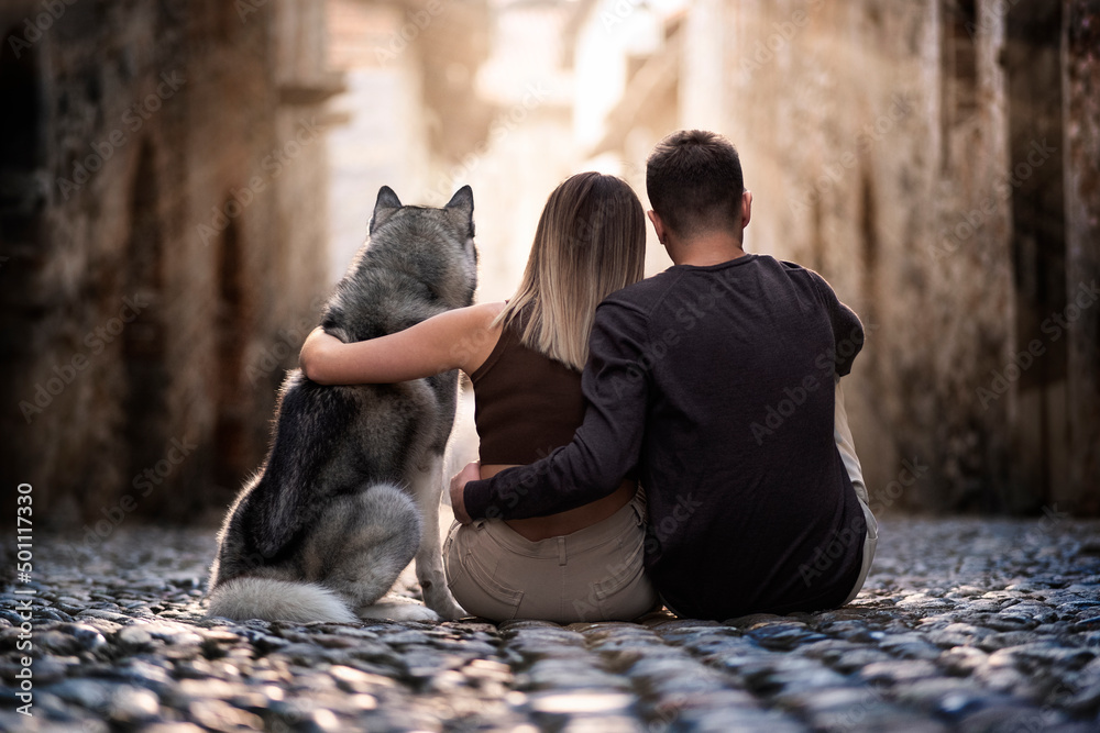 Back view of two young people and their beloved wolf dog sitting and ...