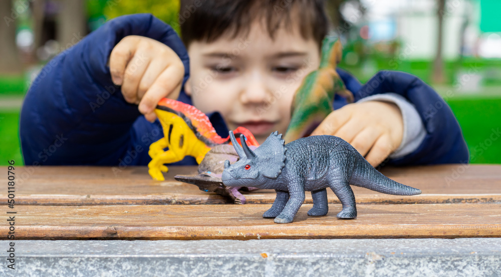 cute kid is playing with dinosaurs toys on park bench, spring, green ...