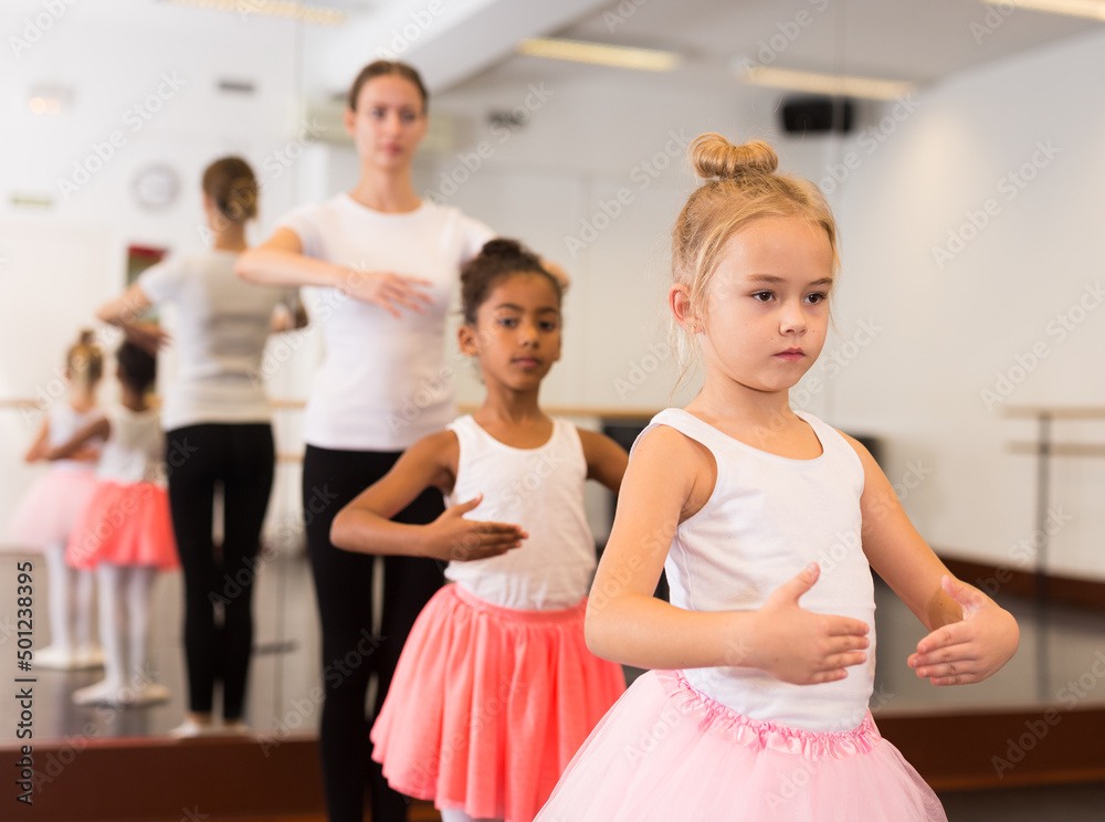 Young female classical dance teacher helping her little girls students ...