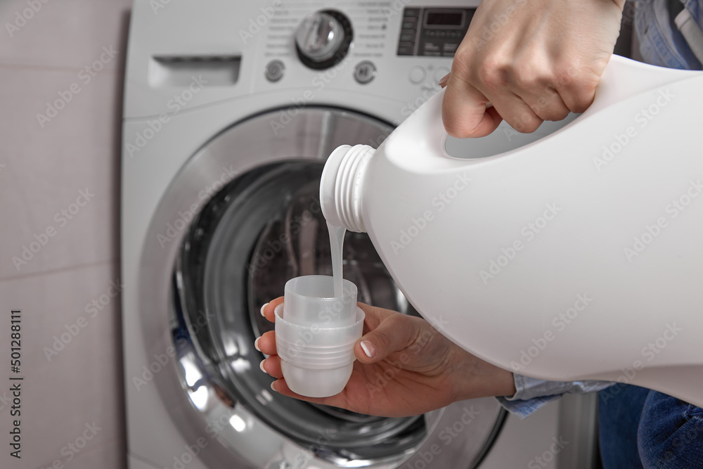 In bathroom where washing machine is located, girl pours the laundry ...