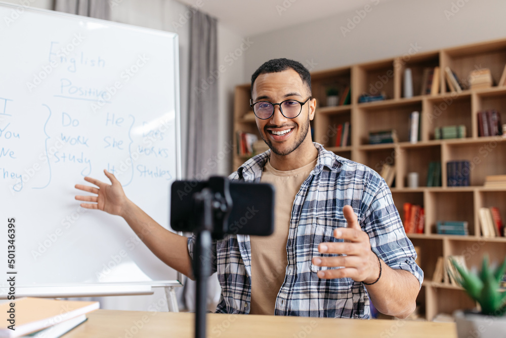 Happy handsome arab male tutor showing rules of english and looking at ...