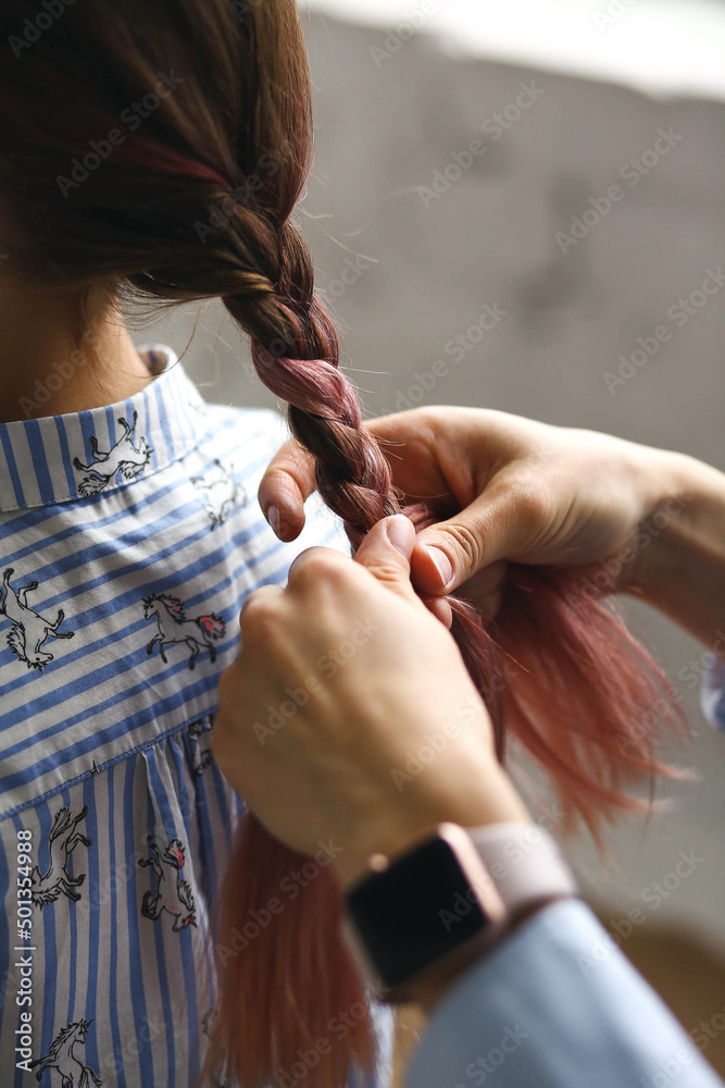 Two girls braid their hair at the window. Mother makes a braid to her ...