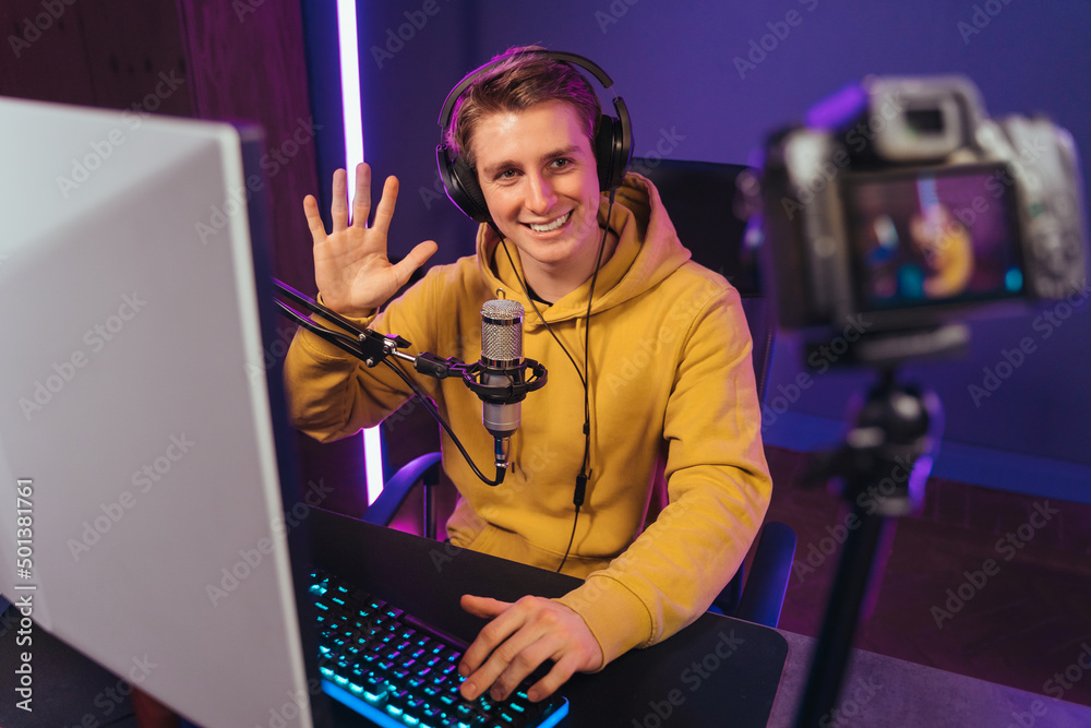 Young handsome vlogger professional gamer waving hand to camera ...