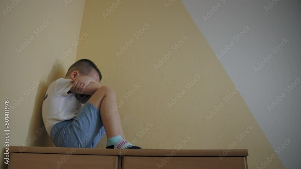 Sad upset little boy sitting in corner hugging knee and crying ...