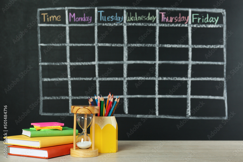 Hourglass and stationery on white wooden table near blackboard with ...