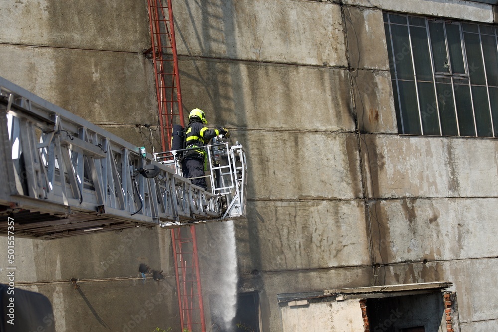 A firefighter from a car ladder truck extinguishes a fire in an ...