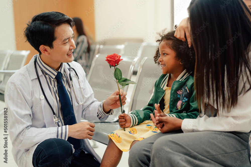 Happy asian doctor giving rose flower to little girl patient while ...