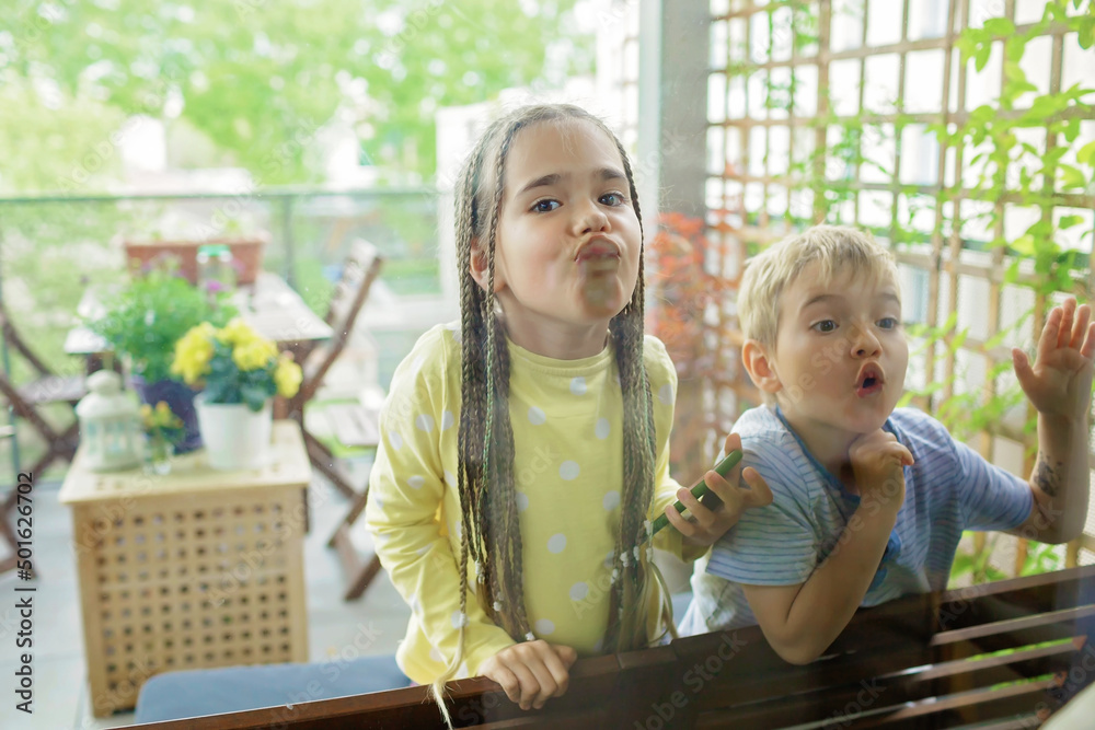 Happy kids have fun and lean against the glass with their faces on cozy ...
