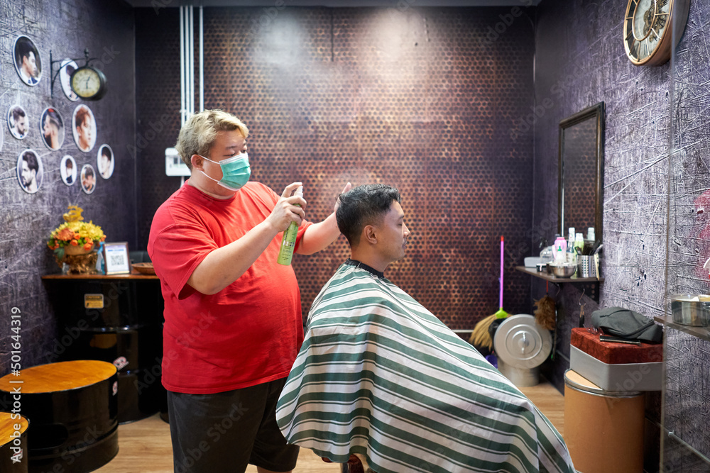 Fat barber putting hairspray in a customer's hair in a barber shop ...